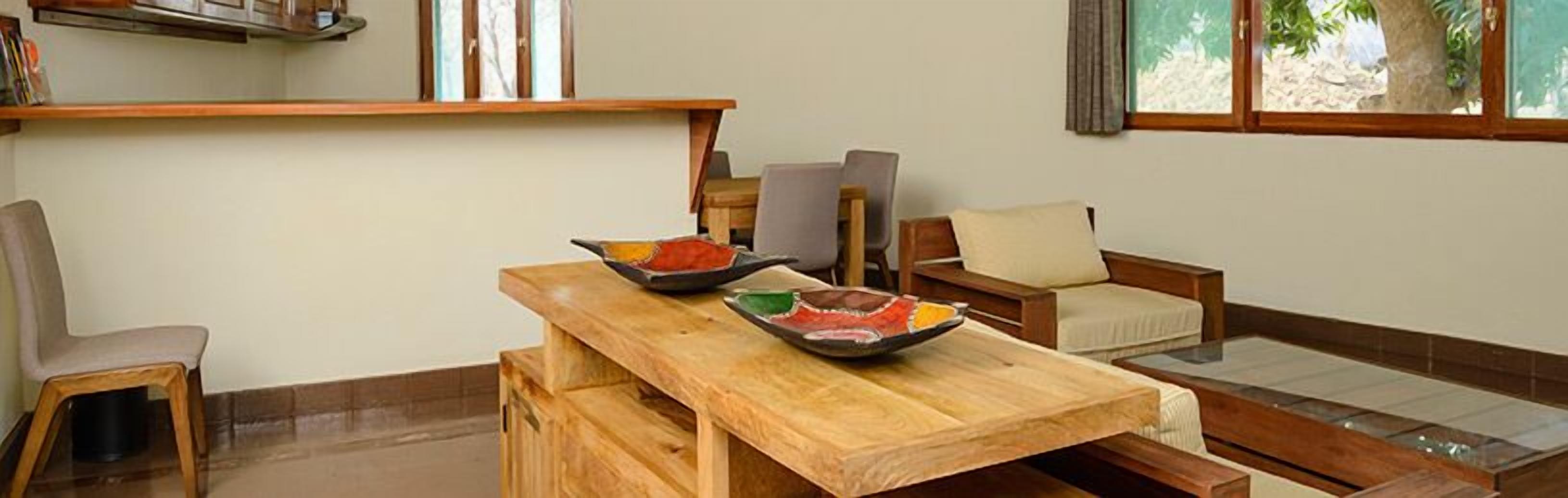 Uma mesa de jantar de madeira com duas tigelas, uma cadeira e um sofá numa divisão com janela e estante.