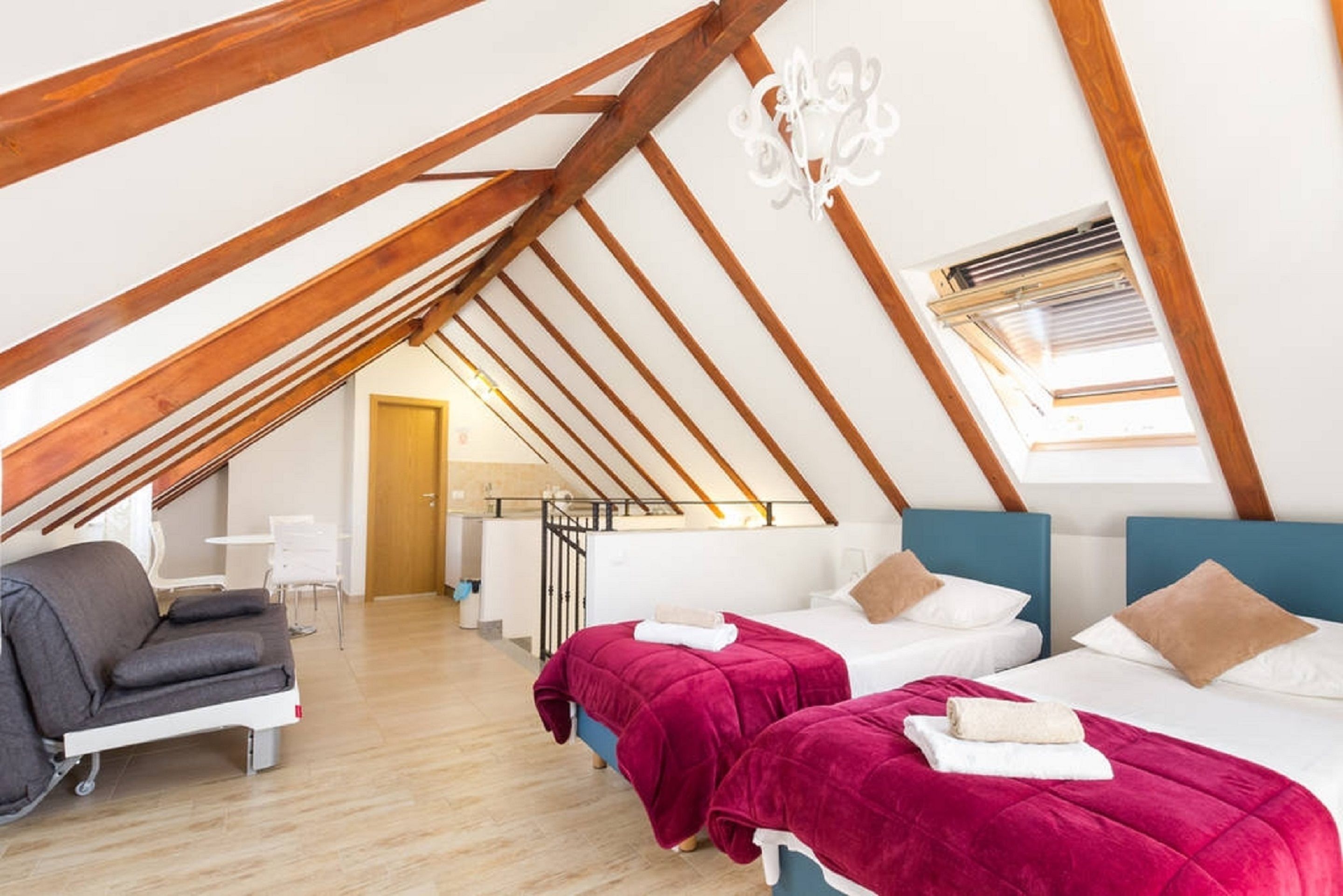 Quarto de sótão acolhedor com vigas de madeira, duas camas com roupa de cama vermelha e branca, um sofá e um candelabro.