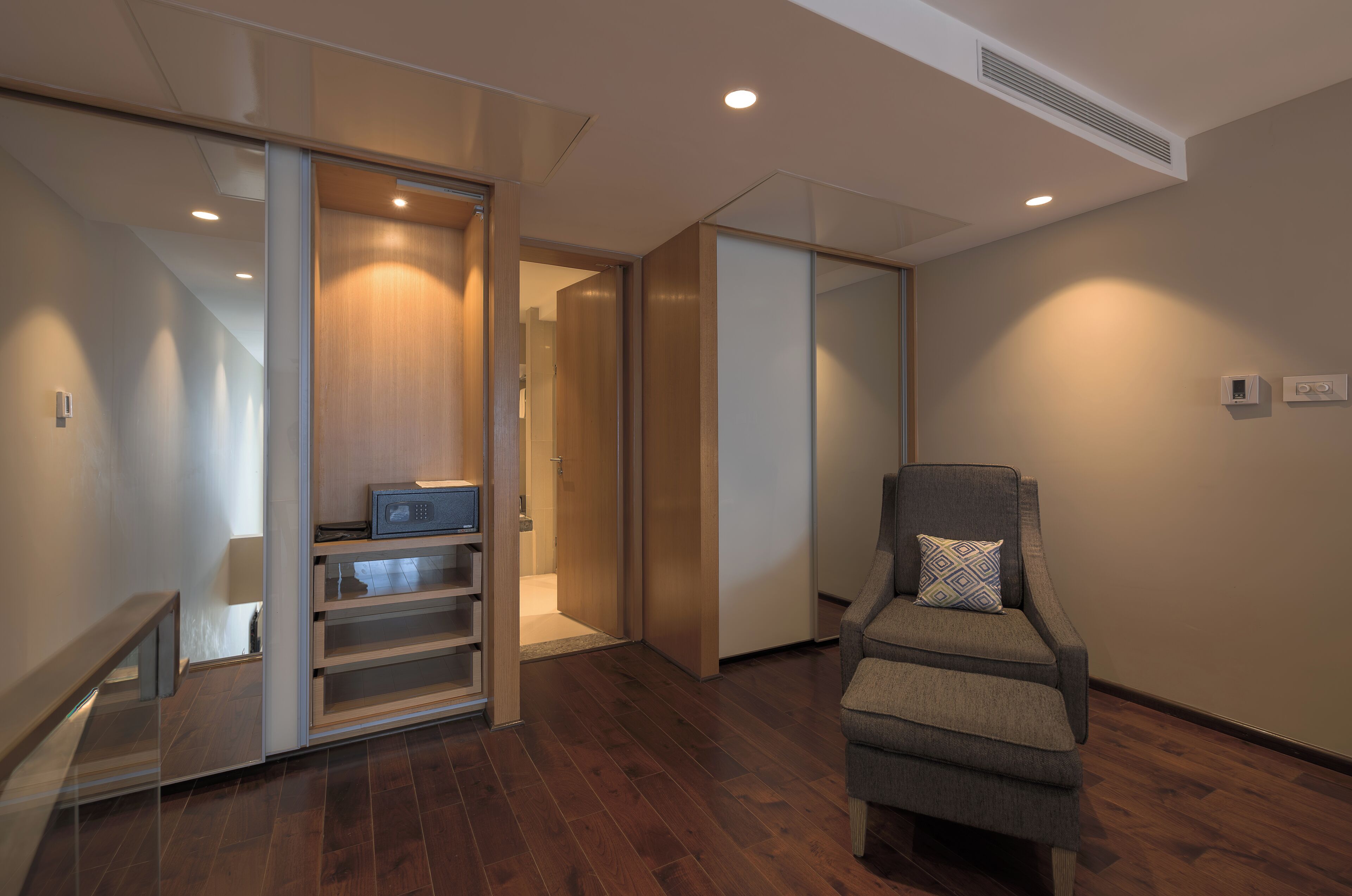 Quarto moderno com closet de porta deslizante, uma poltrona cinza e piso de madeira.