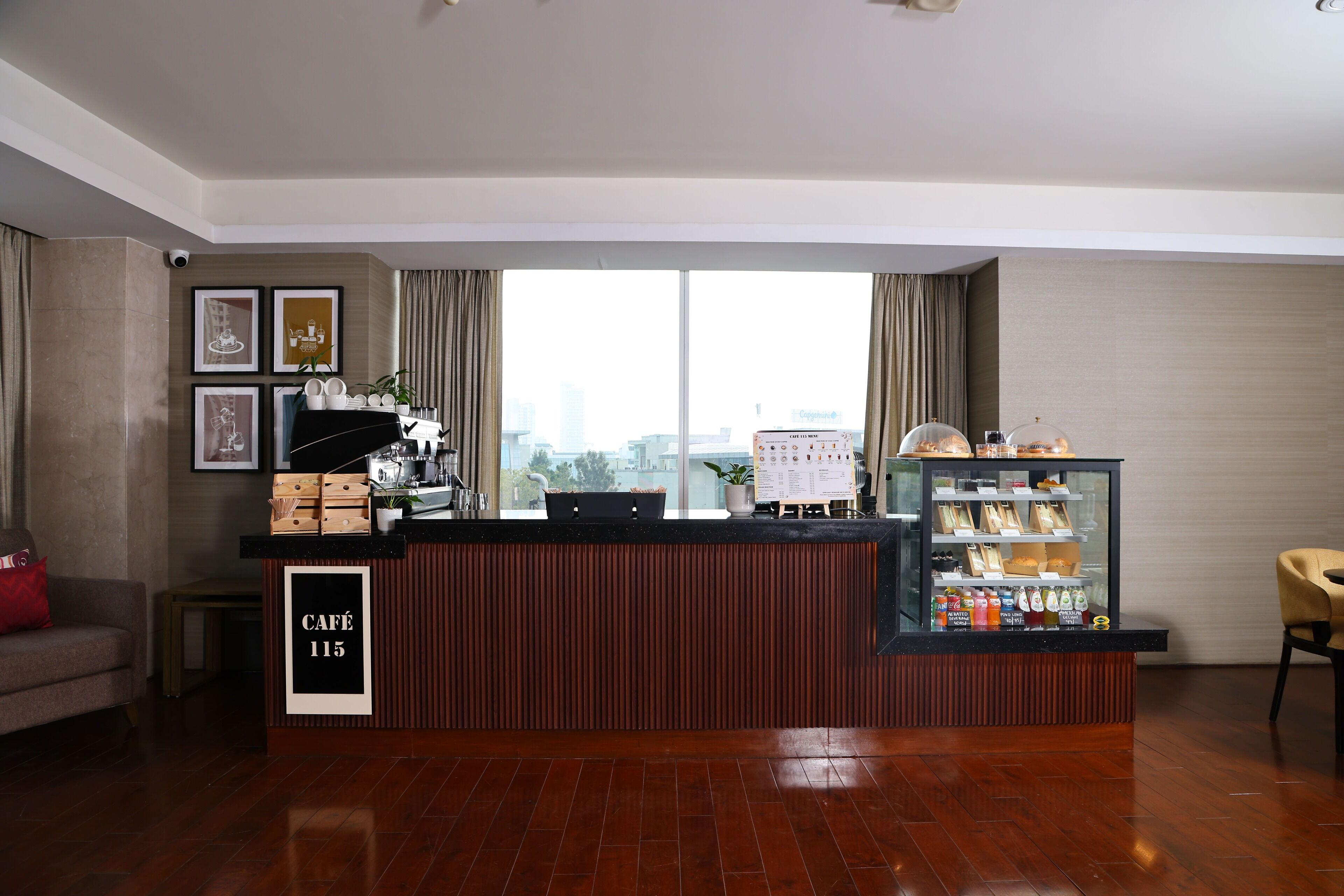 Um saguão moderno de hotel com balcão de recepção, obras de arte emolduradas, um cantinho de café e vista para a cidade.