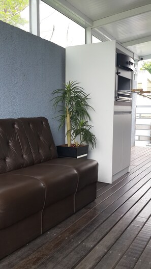 Uma área externa moderna com assento, incluindo um sofá de couro marrom, uma planta em vaso e uma estação de churrasqueira integrada.
