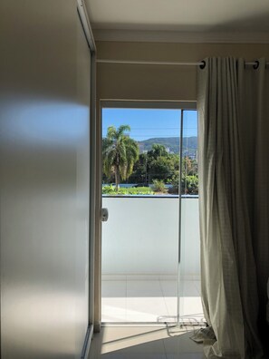 Quarto com porta de vidro deslizante que dá para uma varanda com vista para áreas verdes e edifícios.