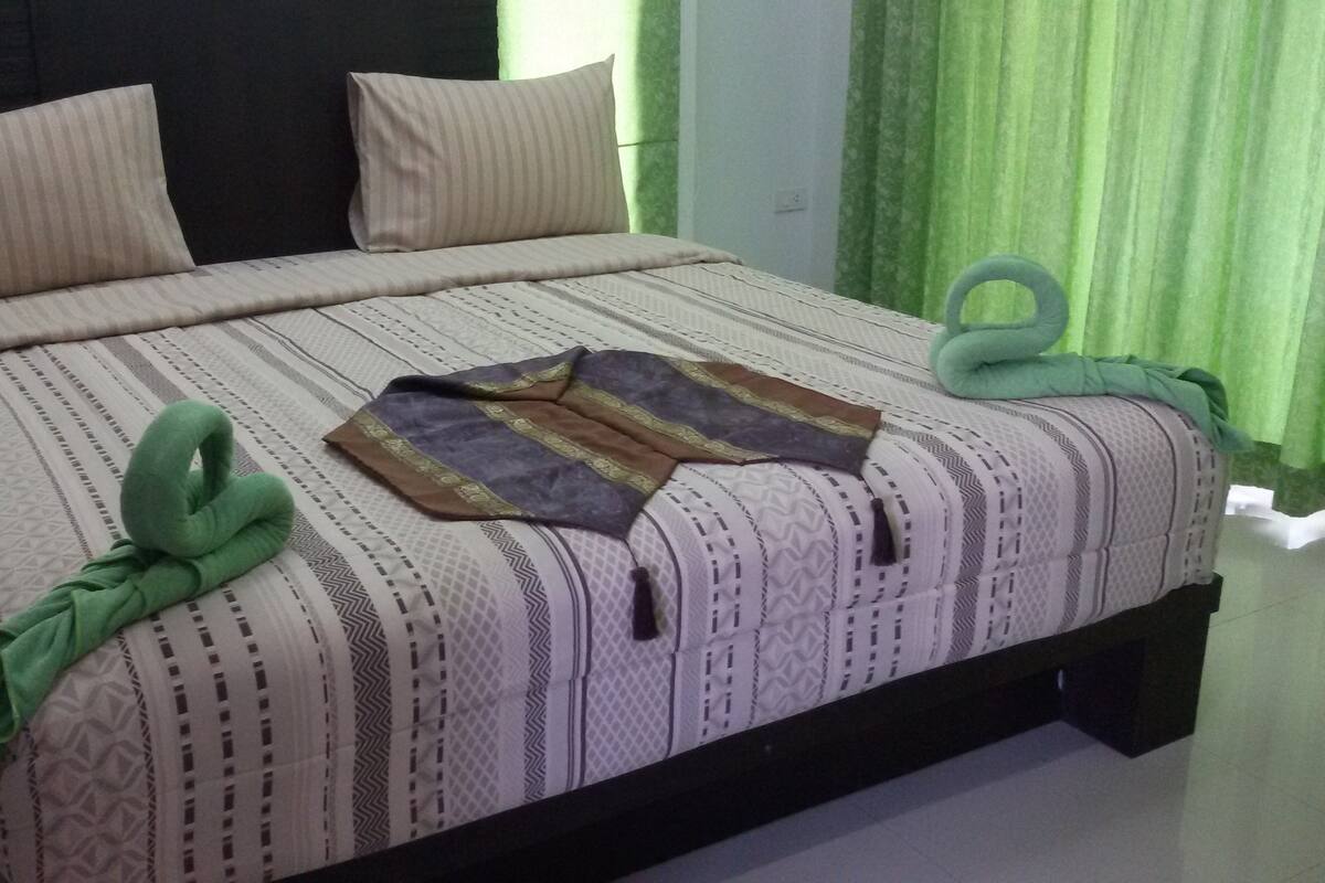 Cama bem arrumada com roupa de cama listrada, travesseiros e um cobertor dobrado.
