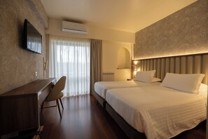 Quarto de hotel com cama, escrivaninha, cadeira, televisão e janela com cortinas.