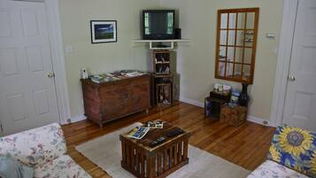Sala de estar com mesa de centro de madeira, televisão em uma estante, espelho e sofás florais.