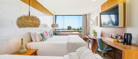 Quarto de hotel com duas camas, uma escrivaninha, televisão e varanda com vista.