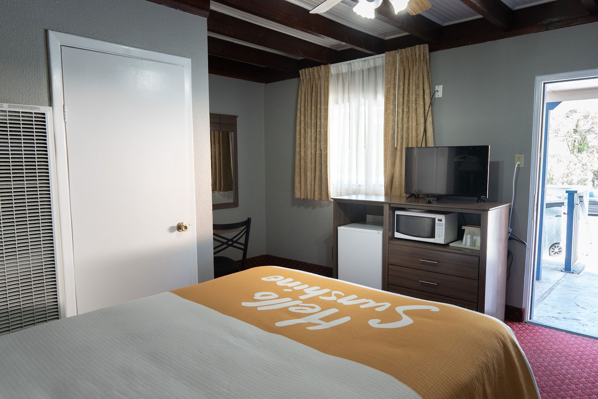 Quarto de hotel com cama, televisão, micro-ondas e porta que dá para área externa.