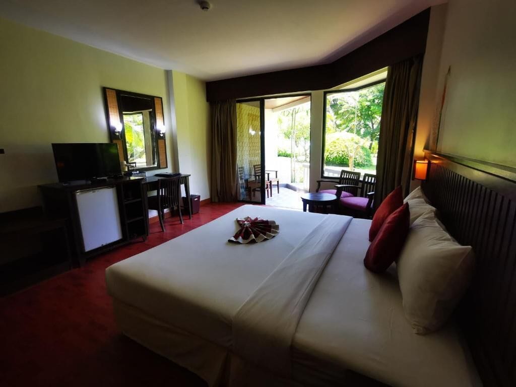 Quarto de hotel com uma cama grande, uma mesa com televisão e vista para o exterior por uma janela ampla.