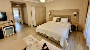 Quarto de hotel com uma cama grande, televisão, mini-frigorífico e guarda-roupa de madeira.