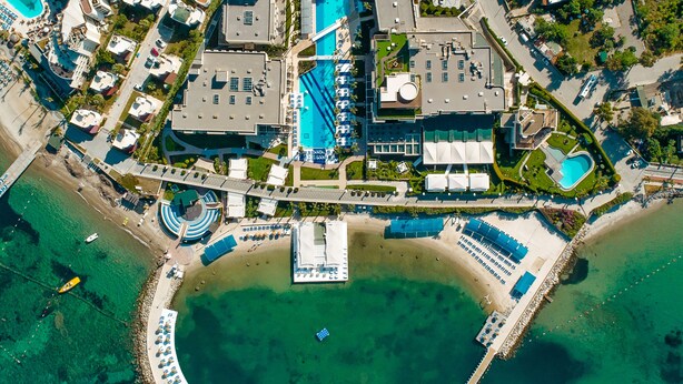Vista aérea de um resort com piscina central, várias unidades de hospedagem e uma área de praia.
