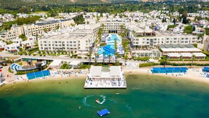 Vista aérea de um resort com piscina central, vários edifícios e área de praia.