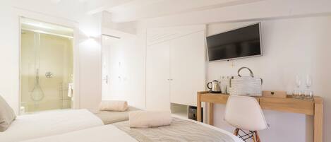 Quarto de hotel moderno com uma cama grande, uma mesa com TV e área de chuveiro.
