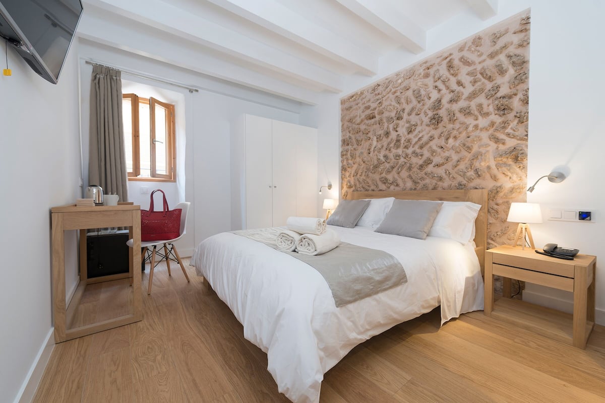 Um quarto com cama, mesas de cabeceira, escrivaninha, cadeira e televisão.