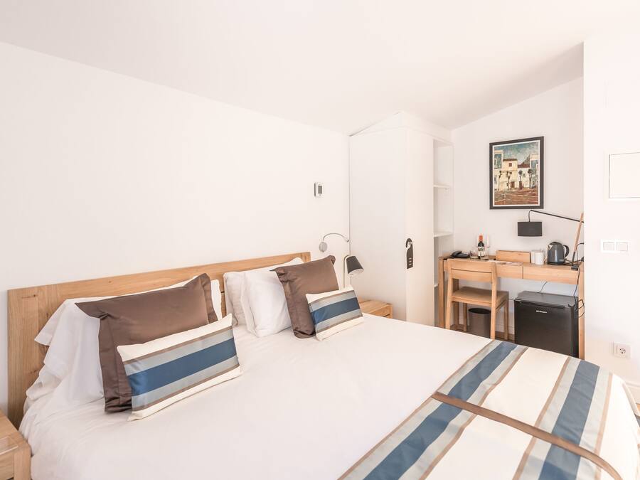 Quarto de hotel com uma cama, uma escrivaninha, uma cadeira, um mini-frigobar e um quadro na parede.