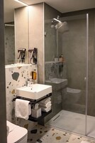 Uma casa de banho moderna com cabine de duche em vidro, lavatório branco e espelho com porta-toalhas.