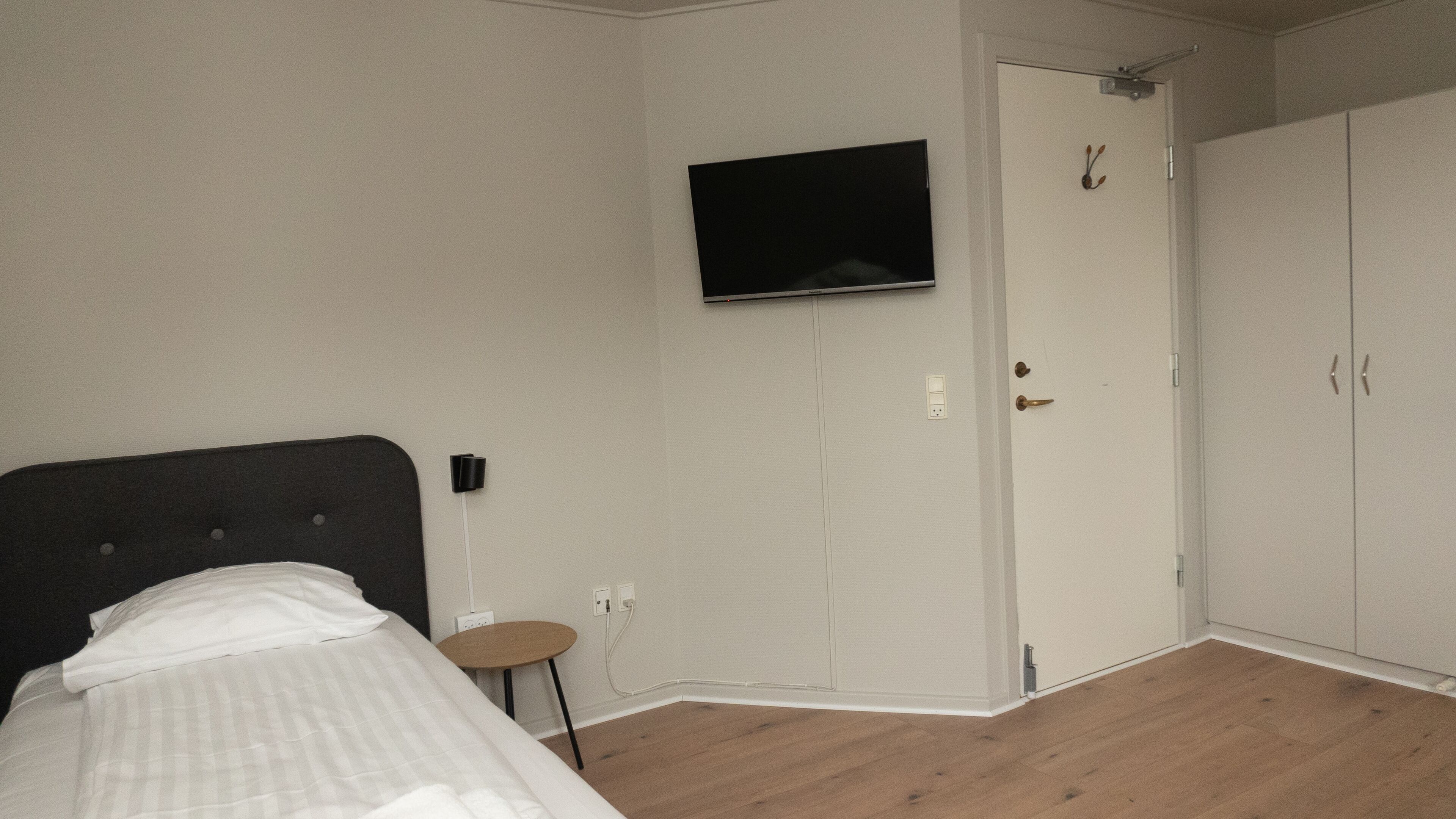 Um quarto com uma cama, televisão na parede, uma porta e um guarda-roupa.