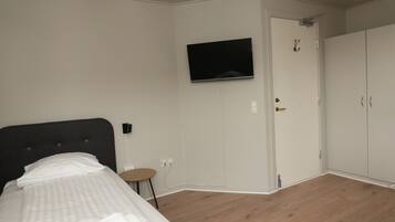 Um quarto com uma cama, televisão na parede, uma porta e um guarda-roupa.