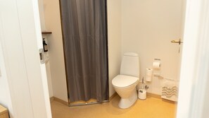 Casa de banho com sanita, cortina de chuveiro, suporte de papel higiénico e secador de mãos.