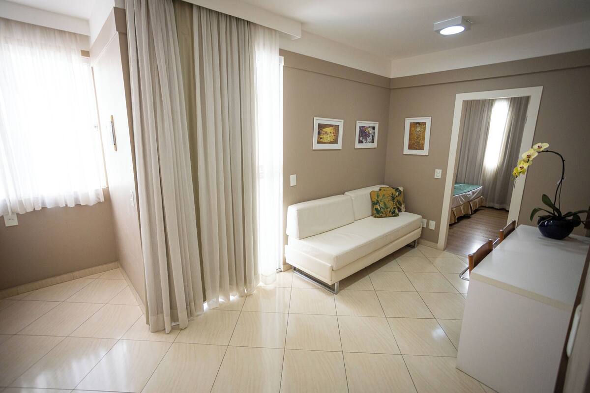 Uma sala de estar moderna com um sofá branco, uma área de refeições com uma mesa branca e um balcão de cozinha.