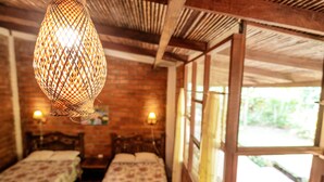 Quarto rústico com duas camas, um lustre pendurado e vista para o verde lá fora.