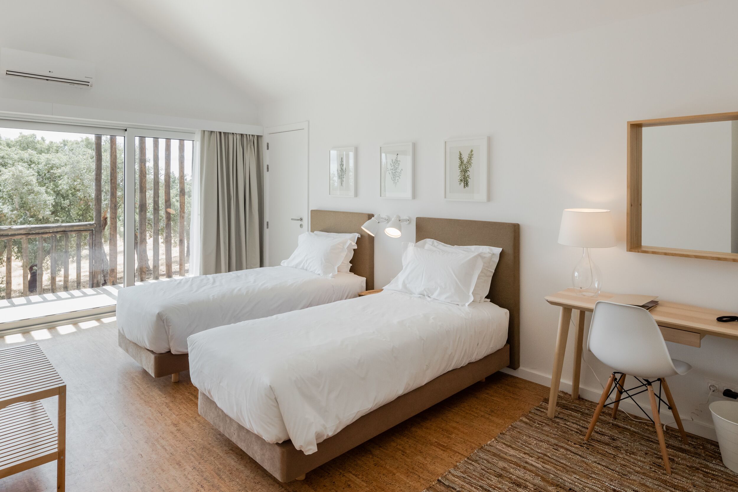 Quarto de hotel com duas camas, uma mesa, uma cadeira e varanda com cortinas.