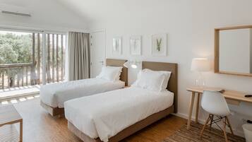 Quarto de hotel com duas camas, uma mesa, uma cadeira e varanda com cortinas.