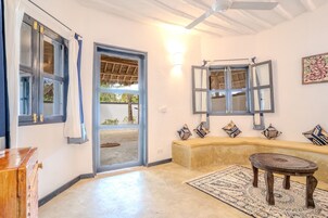 Quarto com sofá, mesa redonda, ventoinha no teto, janela com vista e porta para o exterior.