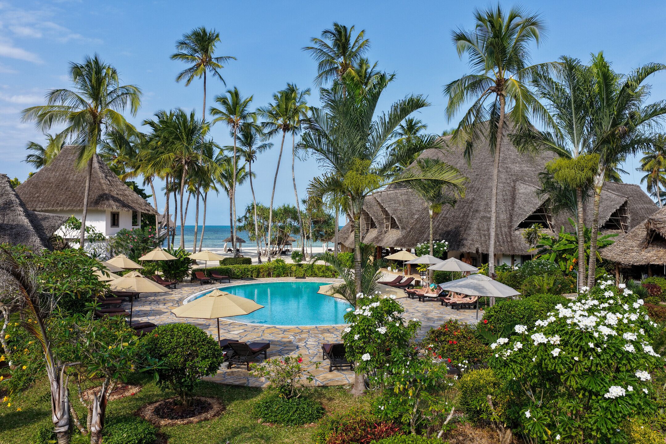 Um resort com piscina, palmeiras e cabanas de telhado de palha.