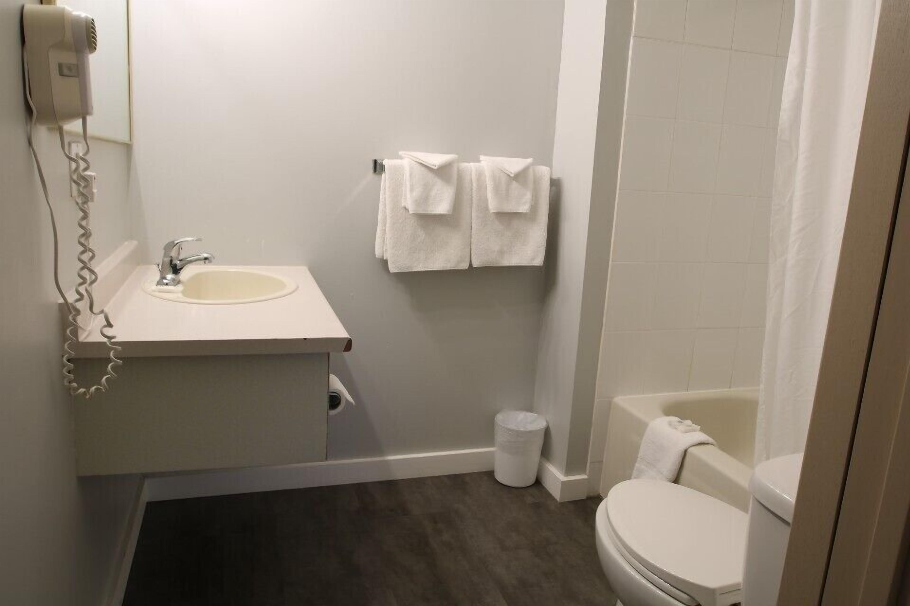 Casa de banho com lavatório, sanita, chuveiro e secador de cabelo preso à parede.