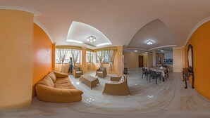 Uma sala de estar ampla, com um sofá grande, cadeiras de vime e uma mesa de jantar.