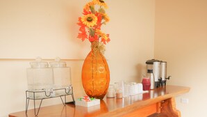 Uma mesa de madeira com um vaso de flores, um dispensador de água e uma cafeteira.