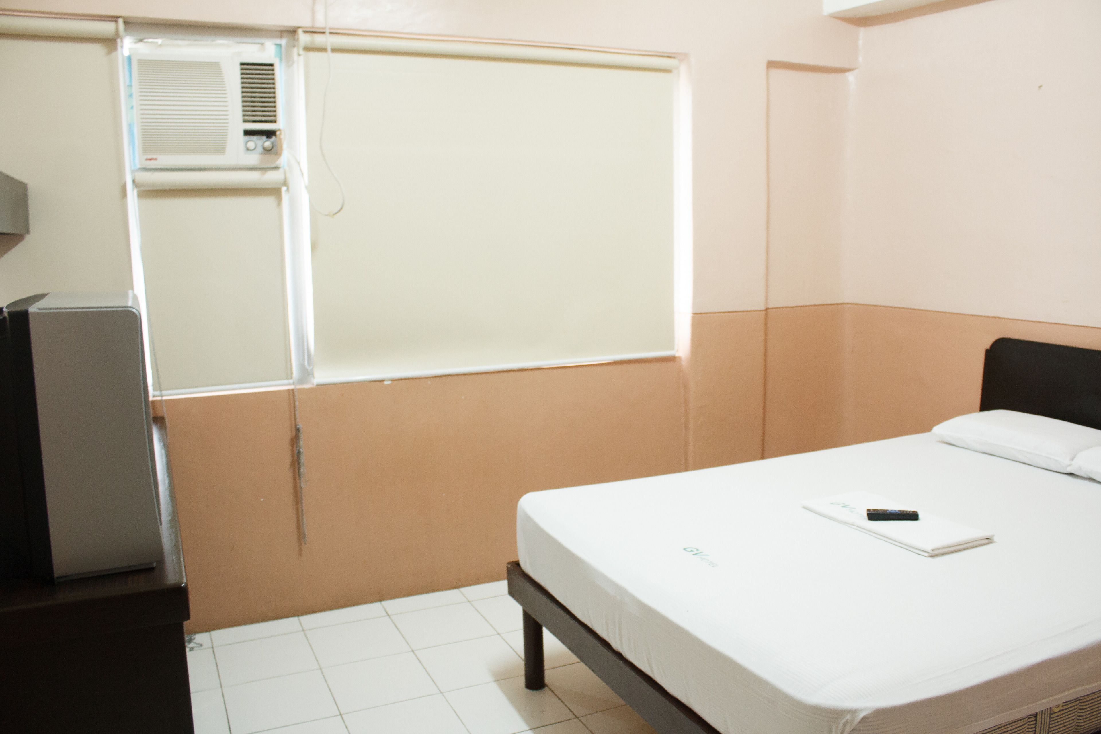 Quarto de hotel com cama, escrivaninha, ar condicionado e janela.