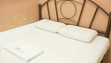 Cama bem arrumada com lençóis e almofadas brancos, uma toalha branca dobrada com o texto "GV Hotel" e uma cabeceira de metal.