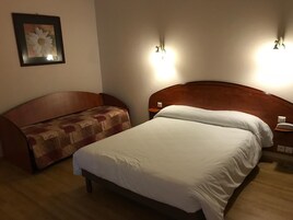Quarto de hotel com cama, sofá e luminária fixada na parede.