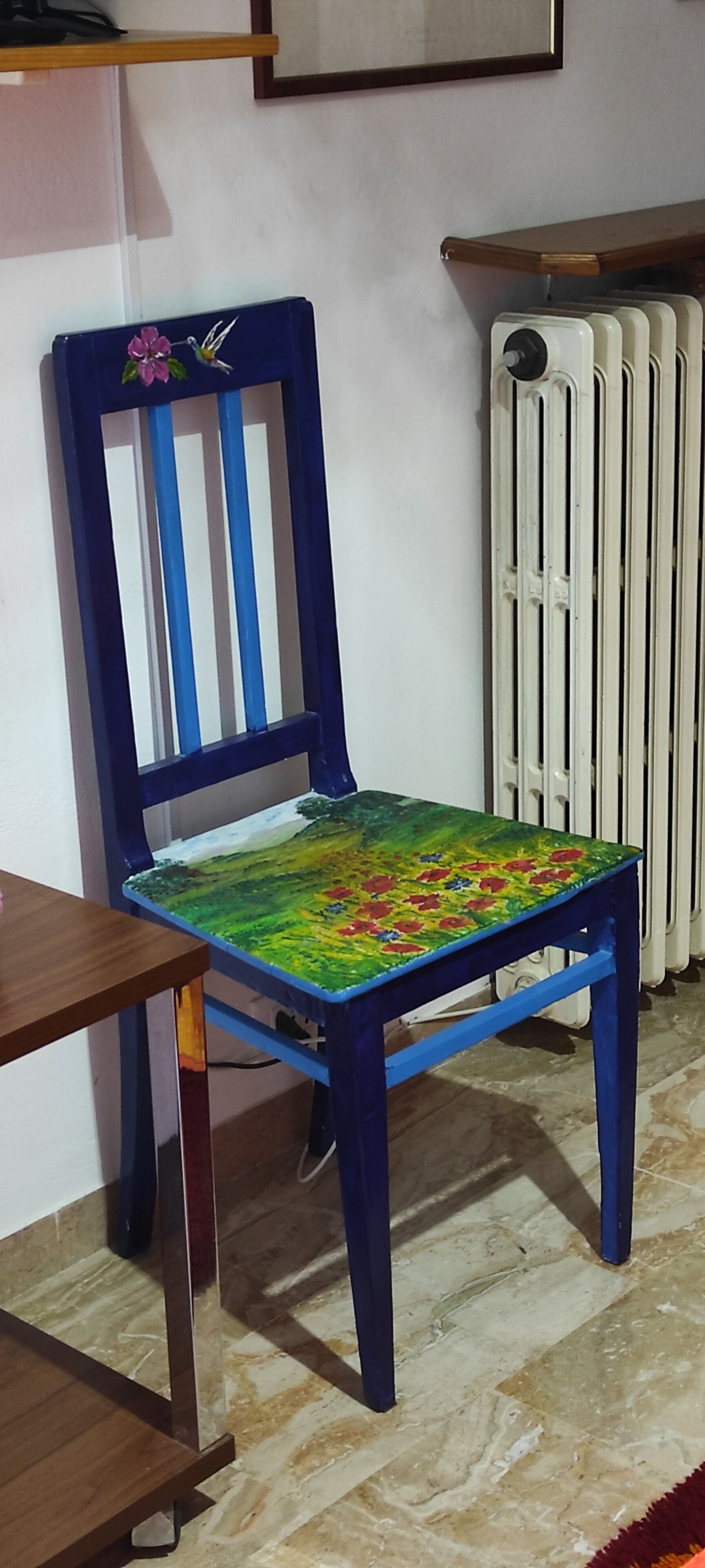 Uma cadeira com assento e encosto coloridos, um radiador e uma mesa de madeira.