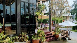 Um restaurante com mesas ao ar livre, plantas em vasos e um espaço coberto tipo varanda.