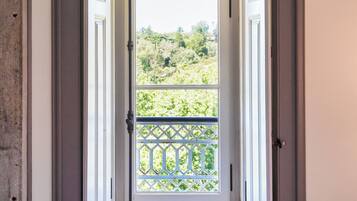 Quarto com uma janela grande, uma cama e vista para o verde lá fora.