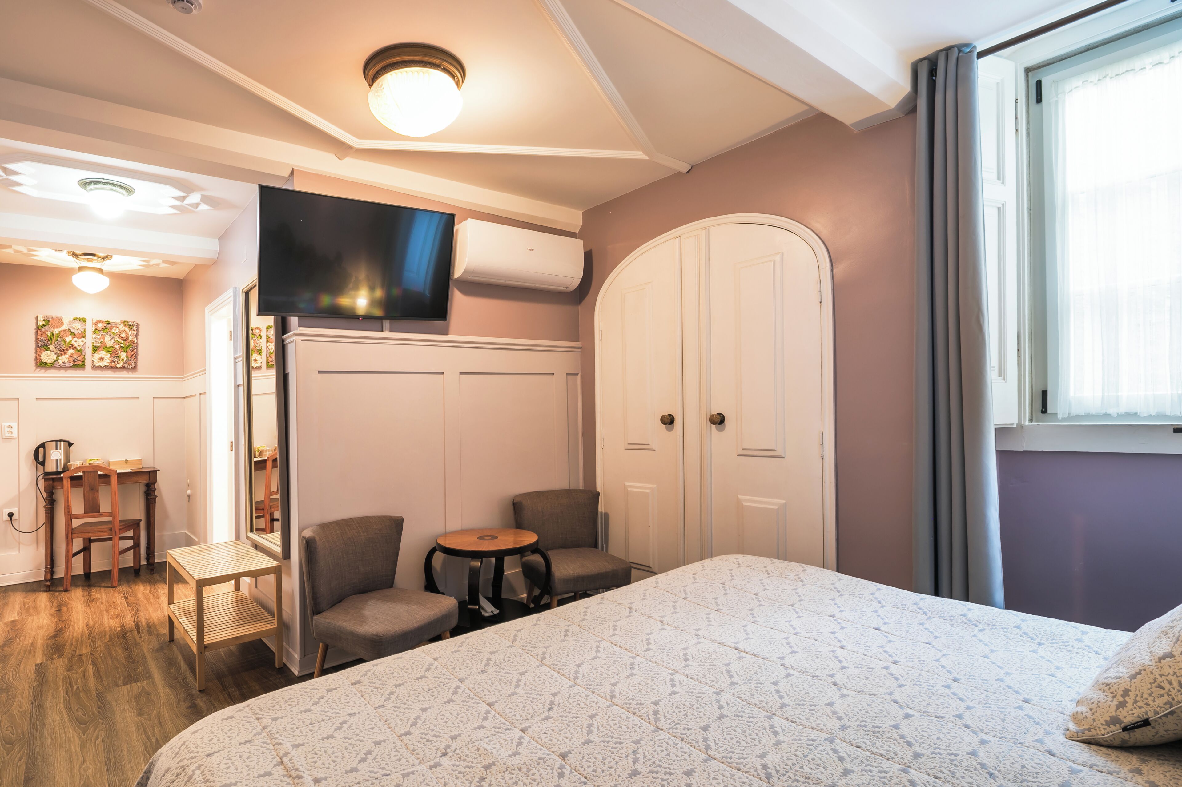 Quarto de hotel com cama, duas cadeiras, uma mesinha, televisão e guarda-roupa.