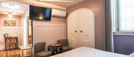 Quarto de hotel com cama, duas cadeiras, uma mesinha, televisão e guarda-roupa.