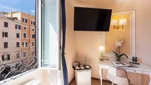Quarto de hotel com uma janela grande, televisão de tela plana, escrivaninha com cadeira e uma pequena mesa de apoio.