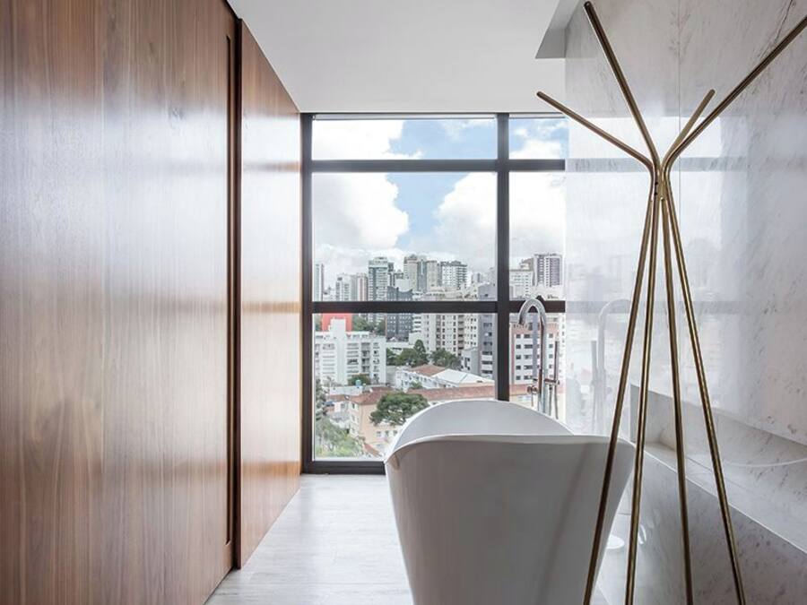 Um interior moderno com uma janela grande, uma banheira branca e um abajur geométrico.
