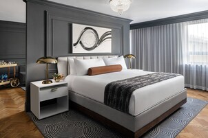 Quarto moderno com uma cama grande, uma mesinha de cabeceira, um abajur decorativo e uma obra de arte na parede.