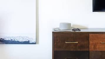 Quarto moderno com uma grande pintura abstrata, cómoda de madeira escura com gavetas, televisão de ecrã plano na parede e um par de sapatos no chão.
