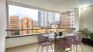 Uma varanda com mesa e cadeiras de vidro, um vaso de planta e vista para a cidade.