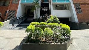 Um hotel moderno com fachada de vidro, um destaque com a placa 'SUITE COMFORT HOTEL' e uma área de jardim bem cuidada em frente.
