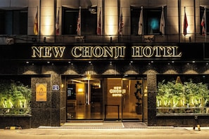 Exterior do Hotel New Chonji com entrada notável, bandeiras e fachada bem iluminada.