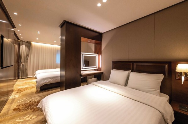 Quarto de hotel com uma cama grande, uma escrivaninha com espelho, televisão e uma luminária na parede.
