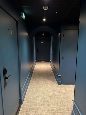 Um corredor com portas numeradas 106 e 108, chão coberto de carpete e uma luminária no teto.