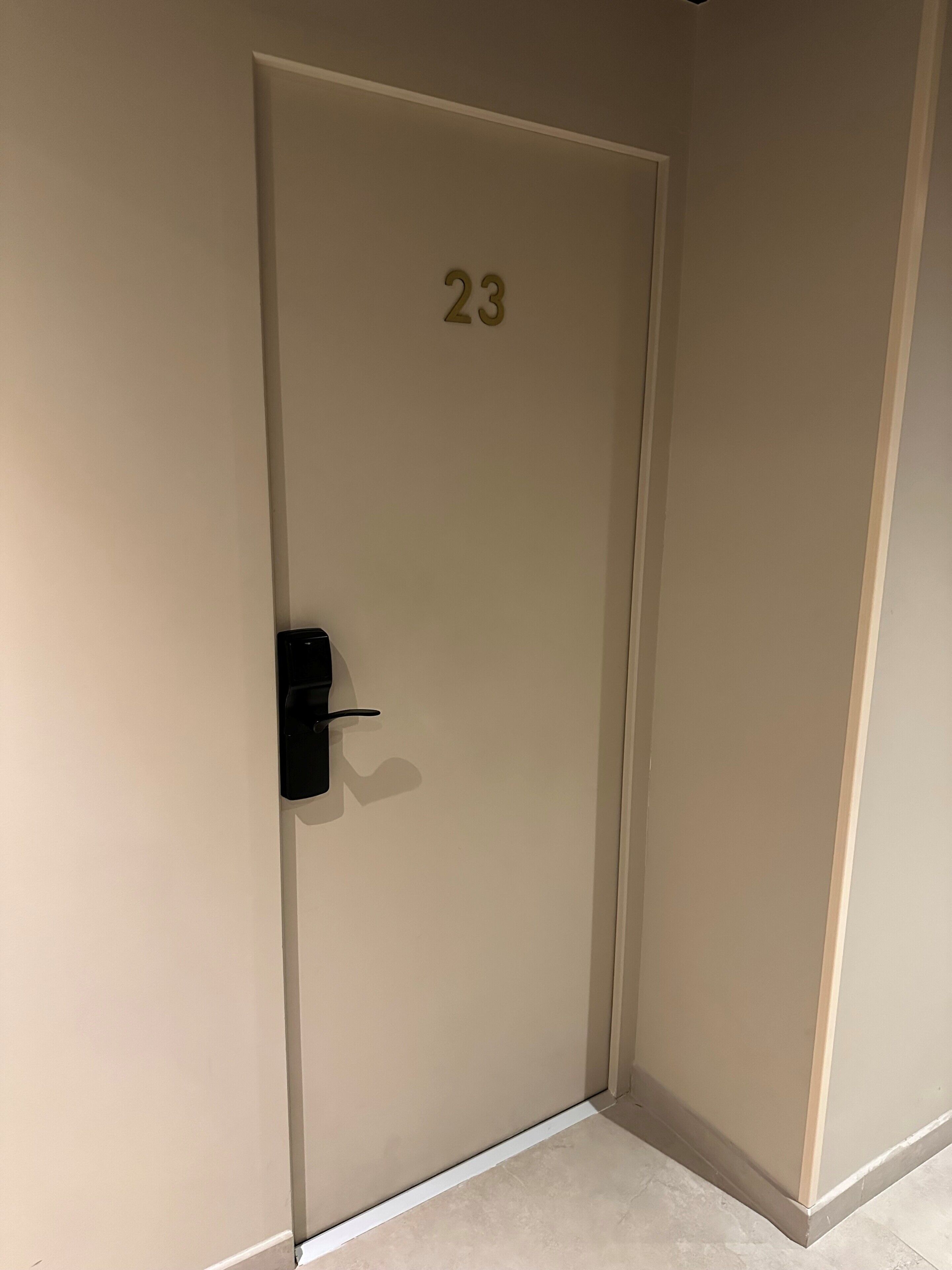 Uma porta fechada com o número 23, uma maçaneta preta e um soleira branca.