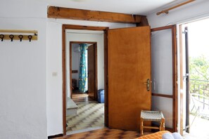 Um quarto com porta de madeira, um pequeno banco e chão de azulejos.